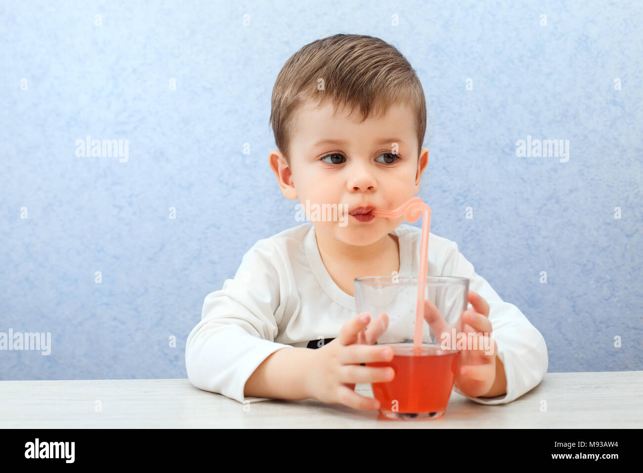 Cute little boy drinking juice on light blue background. Lovely kid ...