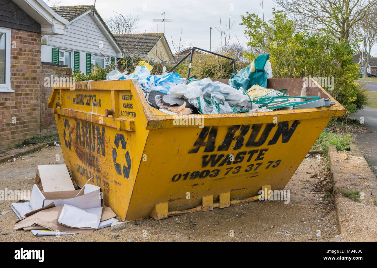 Building waste in a large metallic yellow skip in a driveway in the UK ...