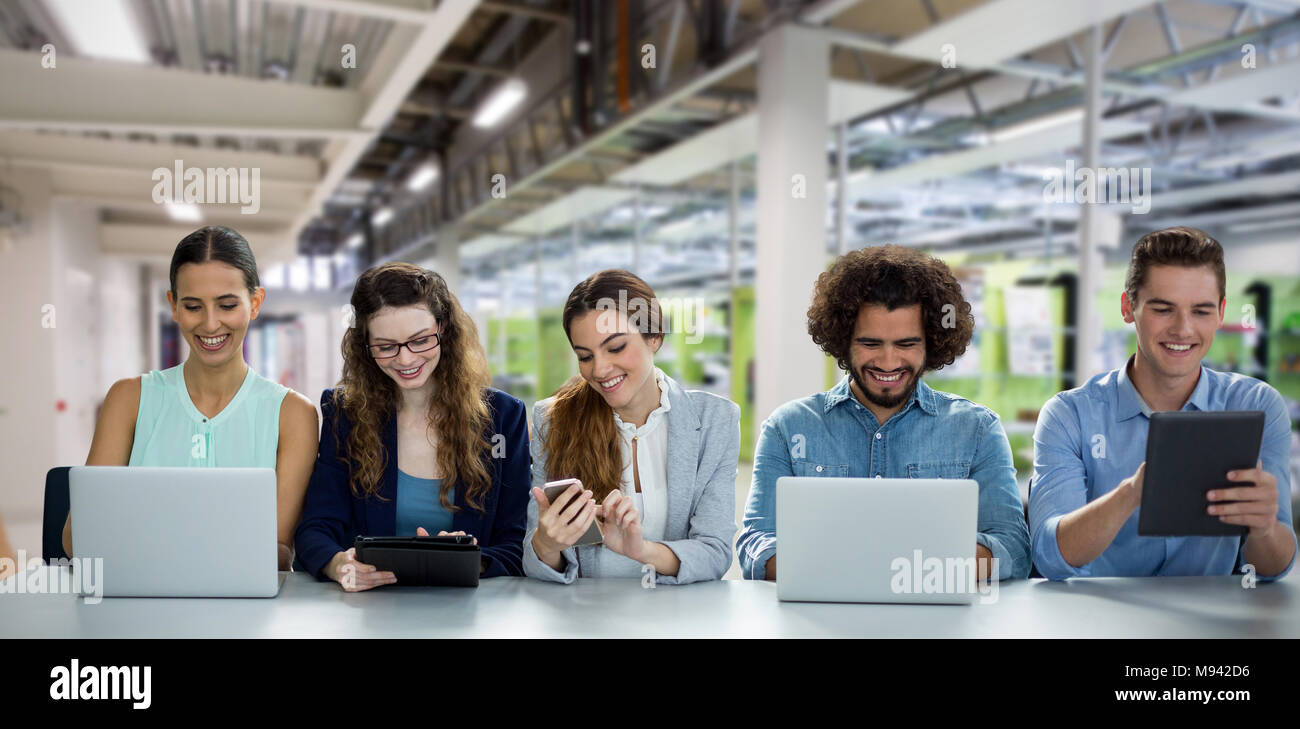 Composite image of colleagues using technology while sitting at table ...