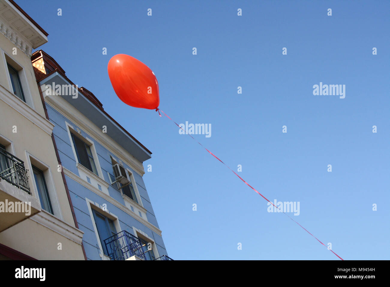 Red balloon floating in the air against the blue sky, part of building ...