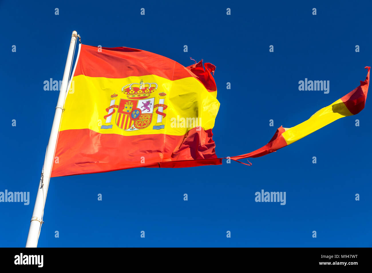 Close-up torn Spanish flag waving on the wind on the mast over clear ...