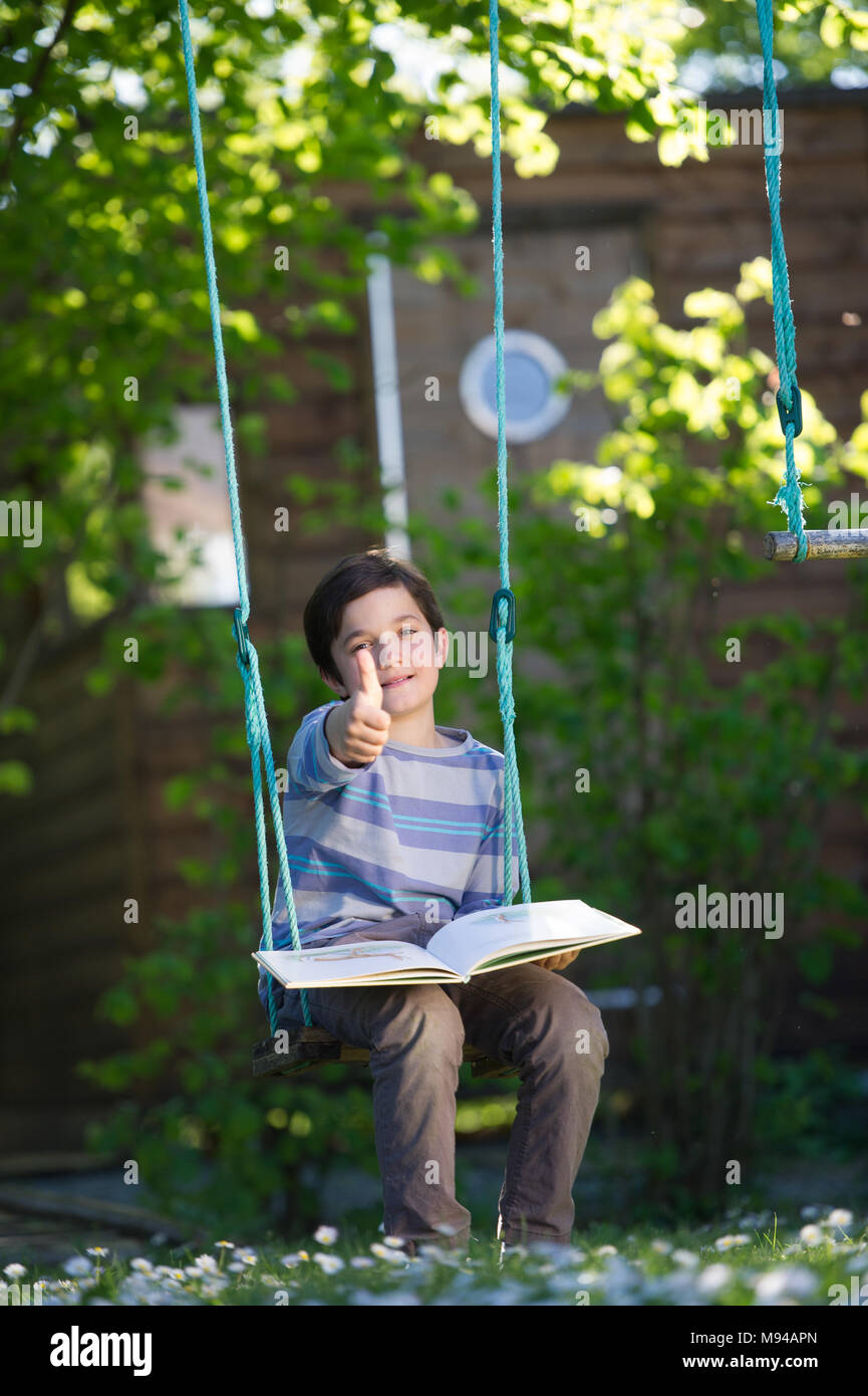 Child reading a book sitting on a swing Stock Photo - Alamy