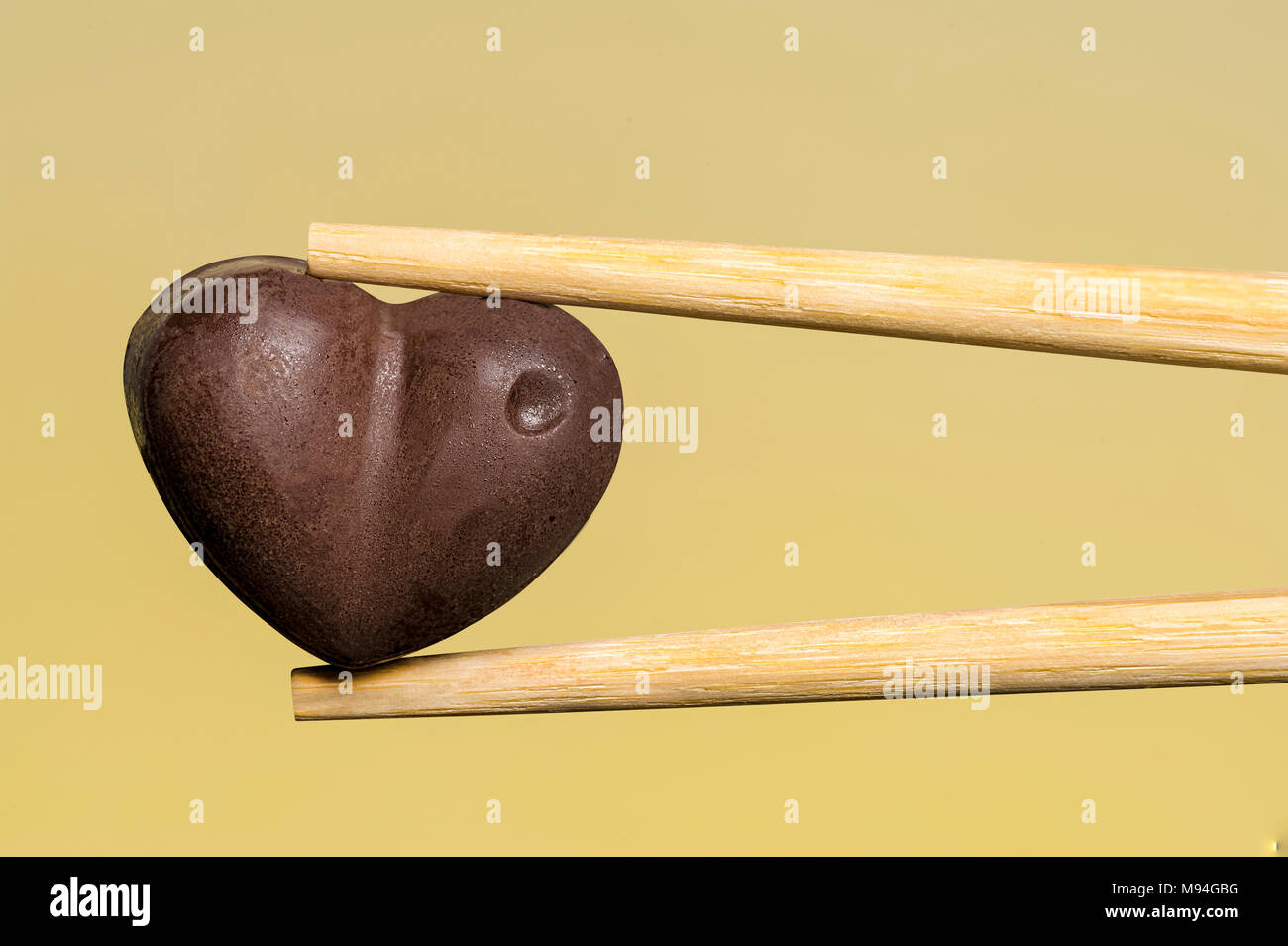 Chinese chopsticks holding a chocolate candy on a yellow background ...