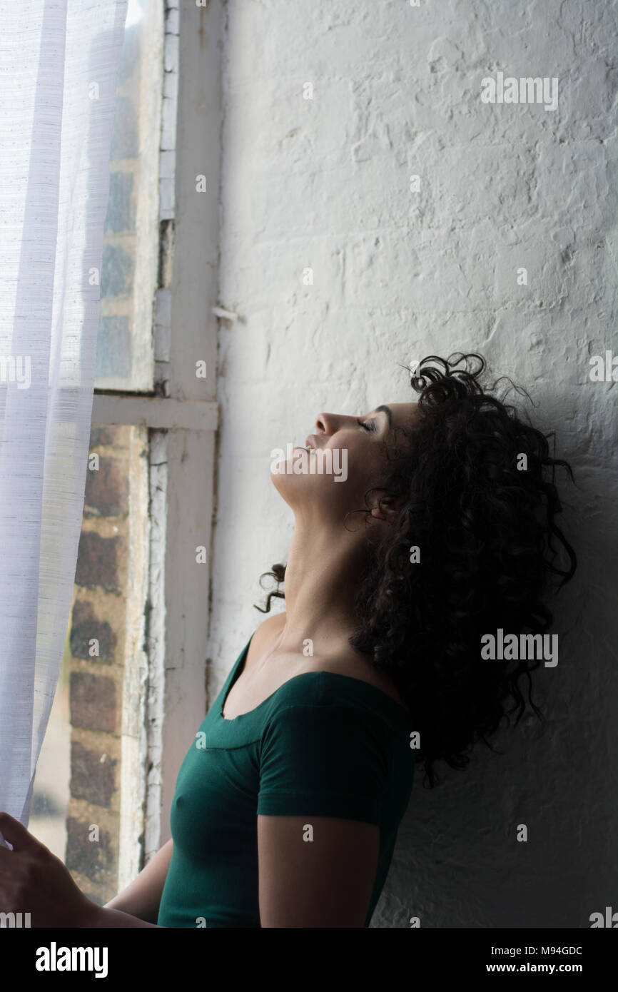Side view of a stressed young woman standing by the window Stock Photo ...
