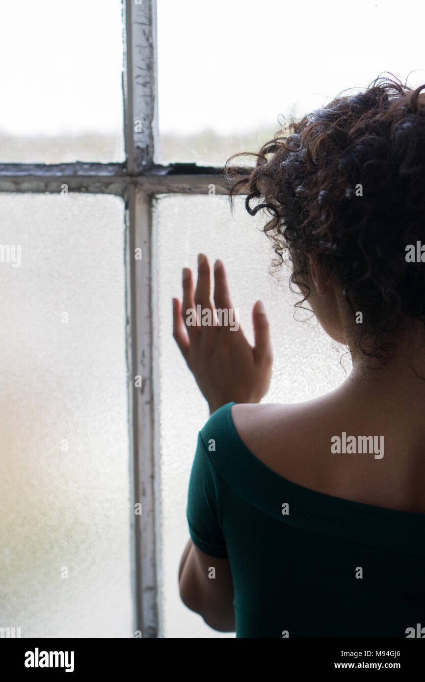 Rear view of a sad young woman standing by the window Stock Photo - Alamy