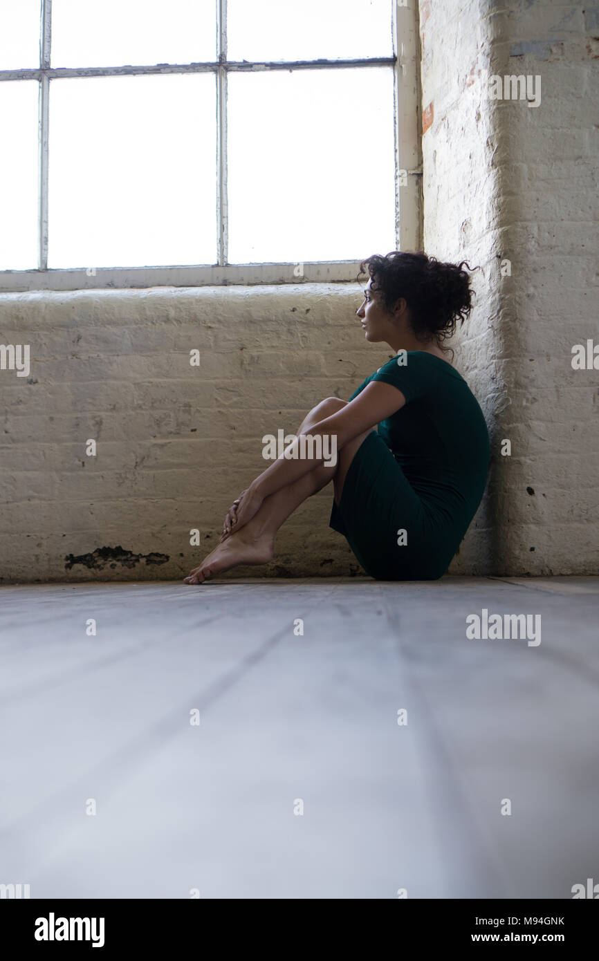 Side view of a sad young woman wearing a dress sat on the floor by the ...