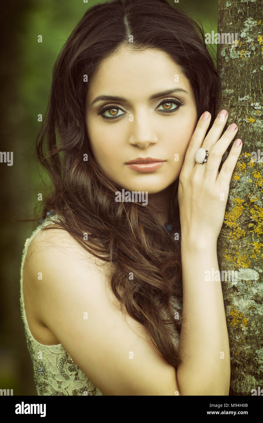Beautiful young woman leaning against a tree Stock Photo - Alamy