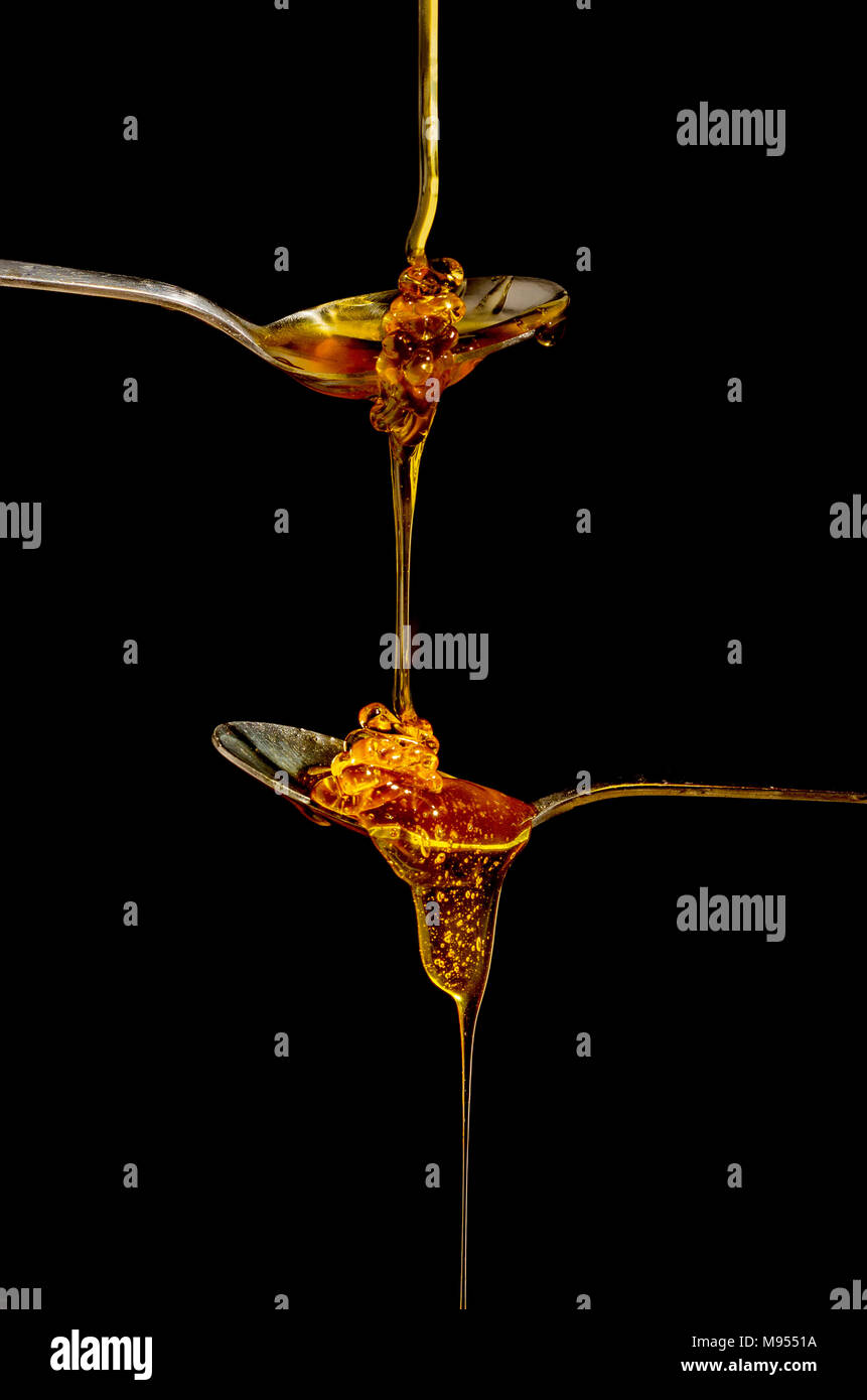 Zwo kitchen spoons with honey dripping on black background Stock Photo ...