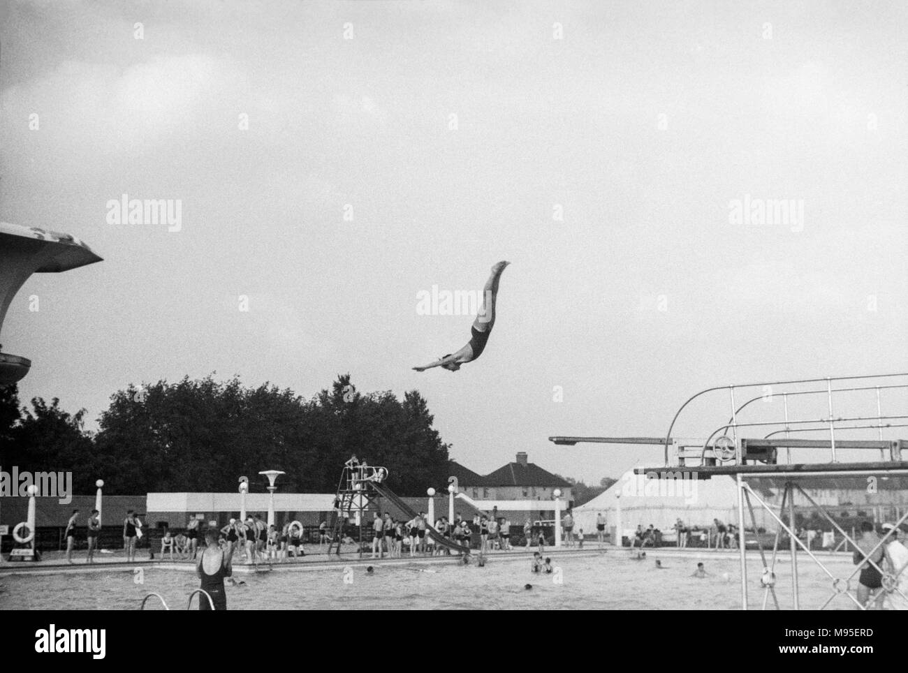 1936. A man dives from a diving board in an outdoor swimming pool in ...