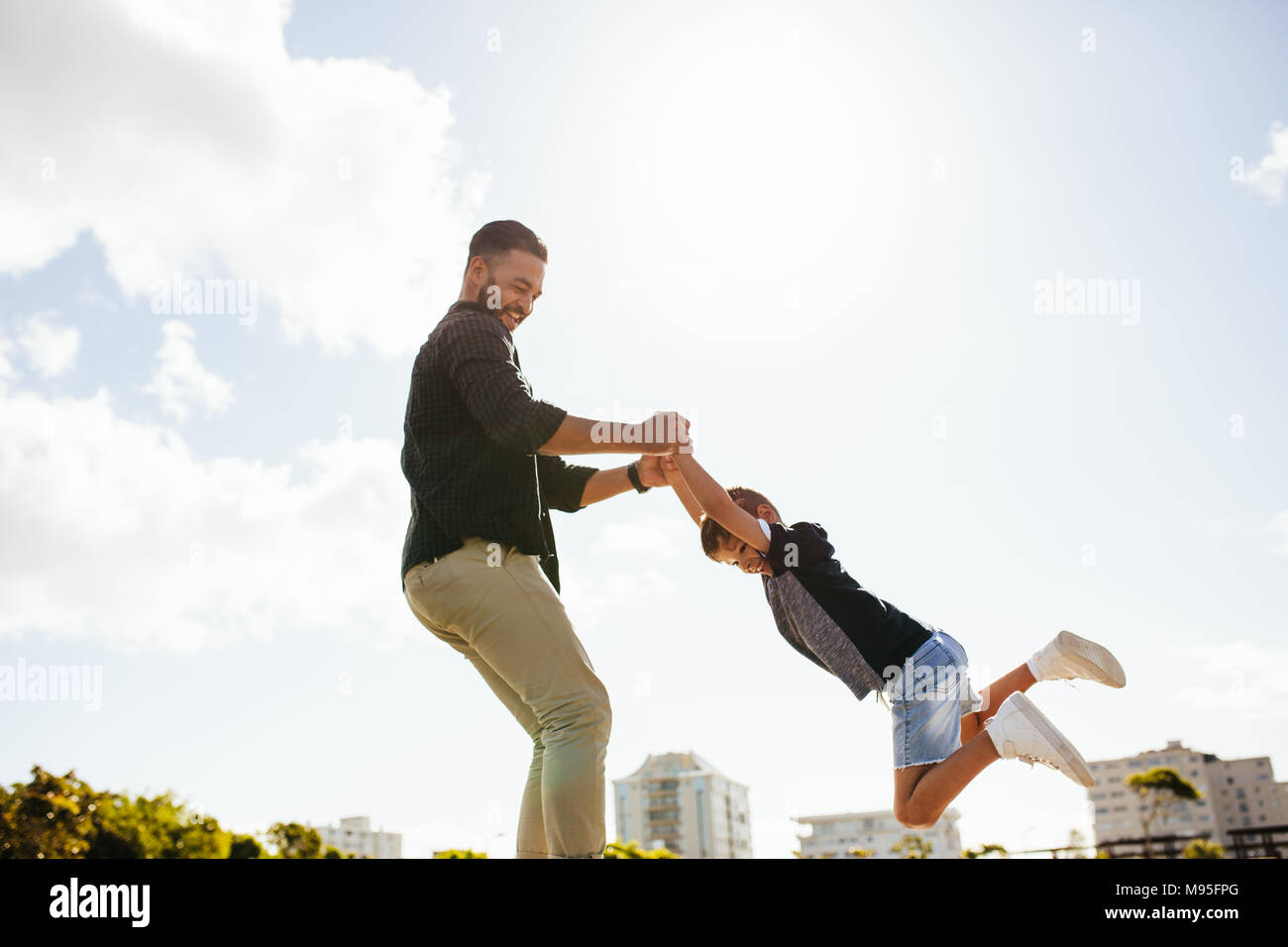 Cheerful man playing with his son at a park. Father lifting his child ...