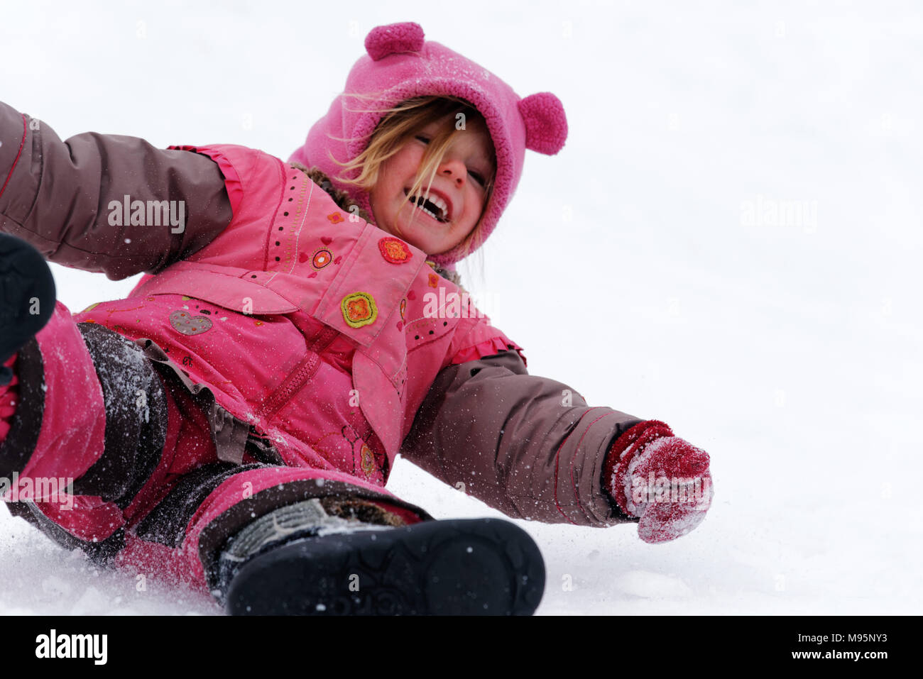A laughing three year old girl sliding on her bum in the snow in Quebec ...