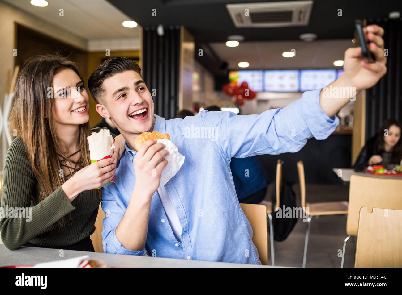 Happy couple eating burger and doner taking selfie together in fast ...