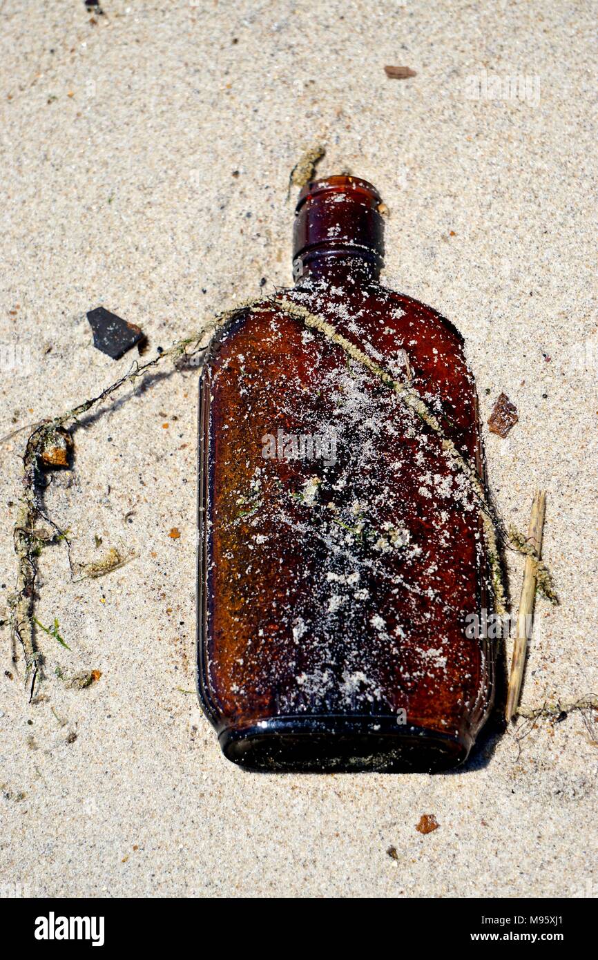 Half-pint liquor bottle washed up on a beach, partly covered with sand ...