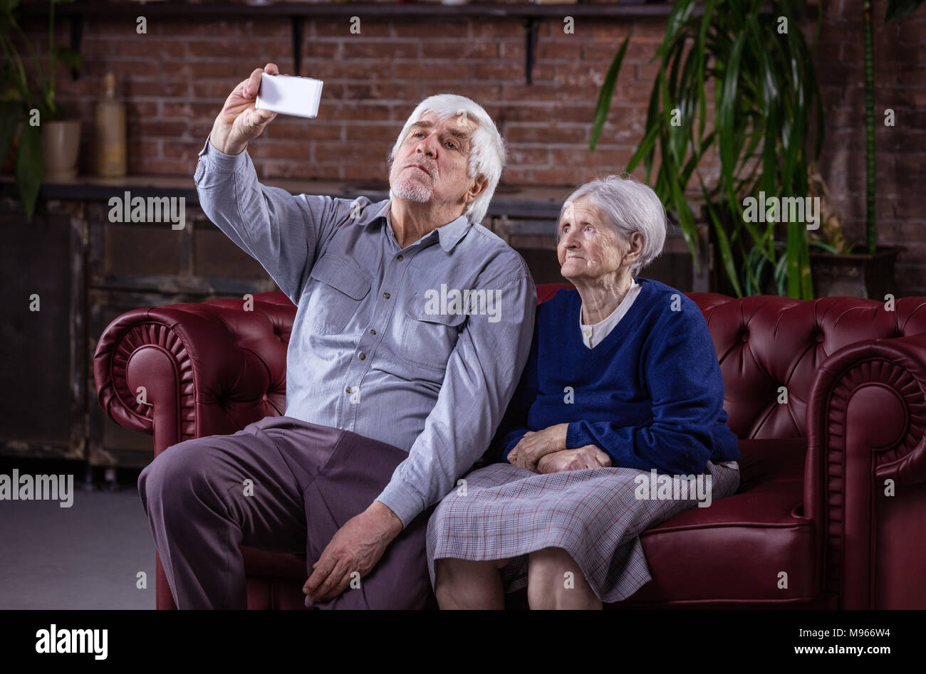 Senior Couple Taking Selfie With Smart Phone While Sitting On Couch At