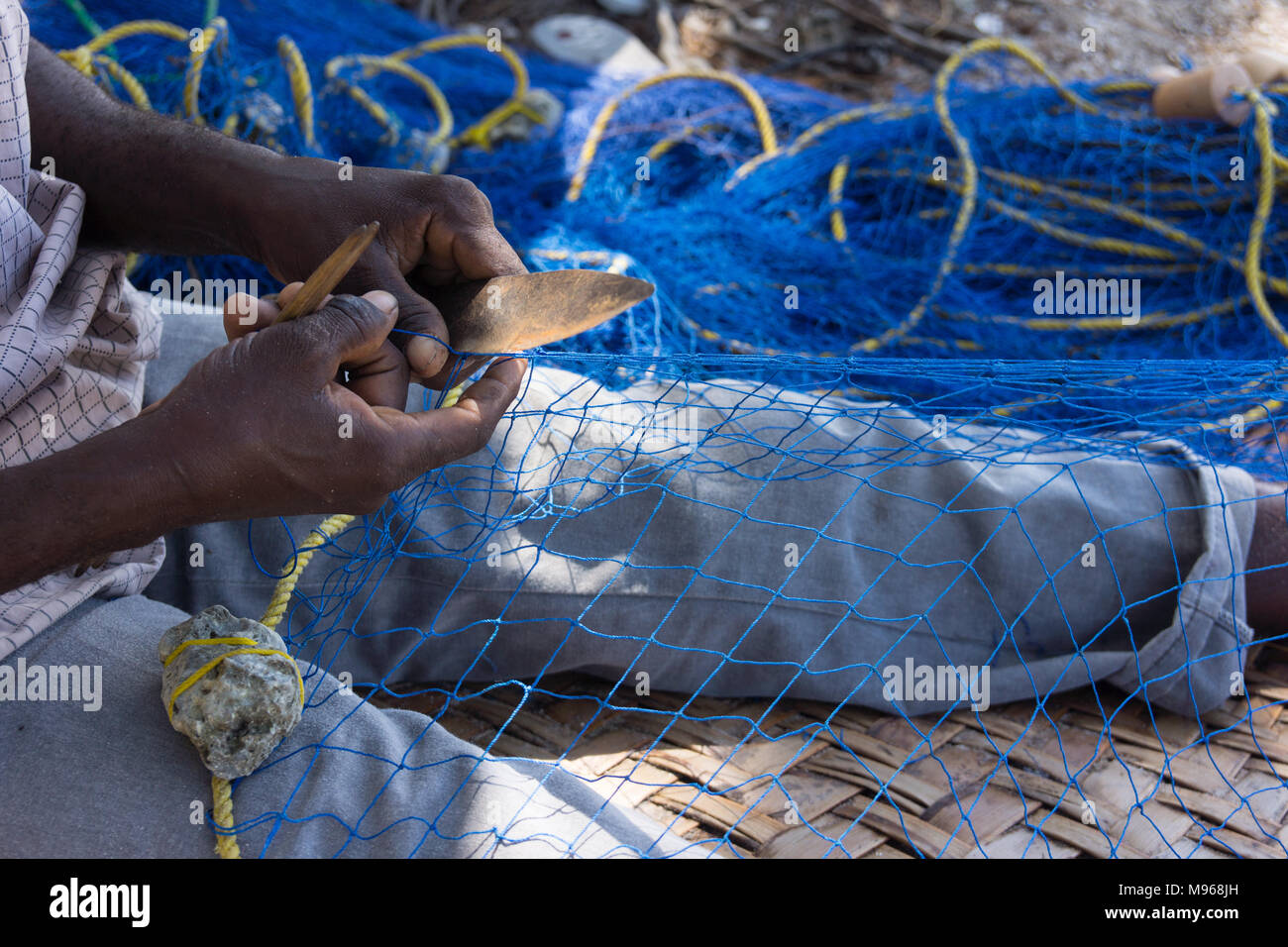 Man on Uzi Island, Zanzibar, mending fishing nets by hand at the beach ...