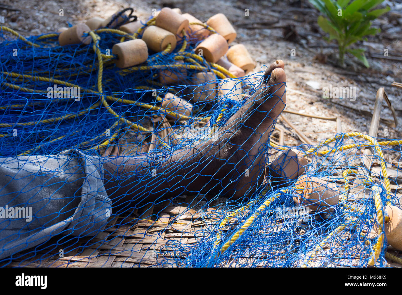 Man on Uzi Island, Zanzibar, mending fishing nets by hand at the beach ...