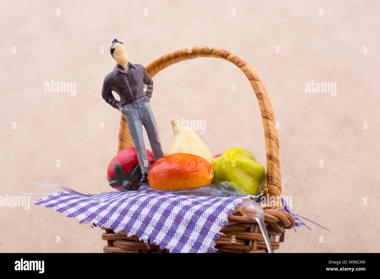Tiny man figurine on a wicker basket with a plastic fruit on a white ...