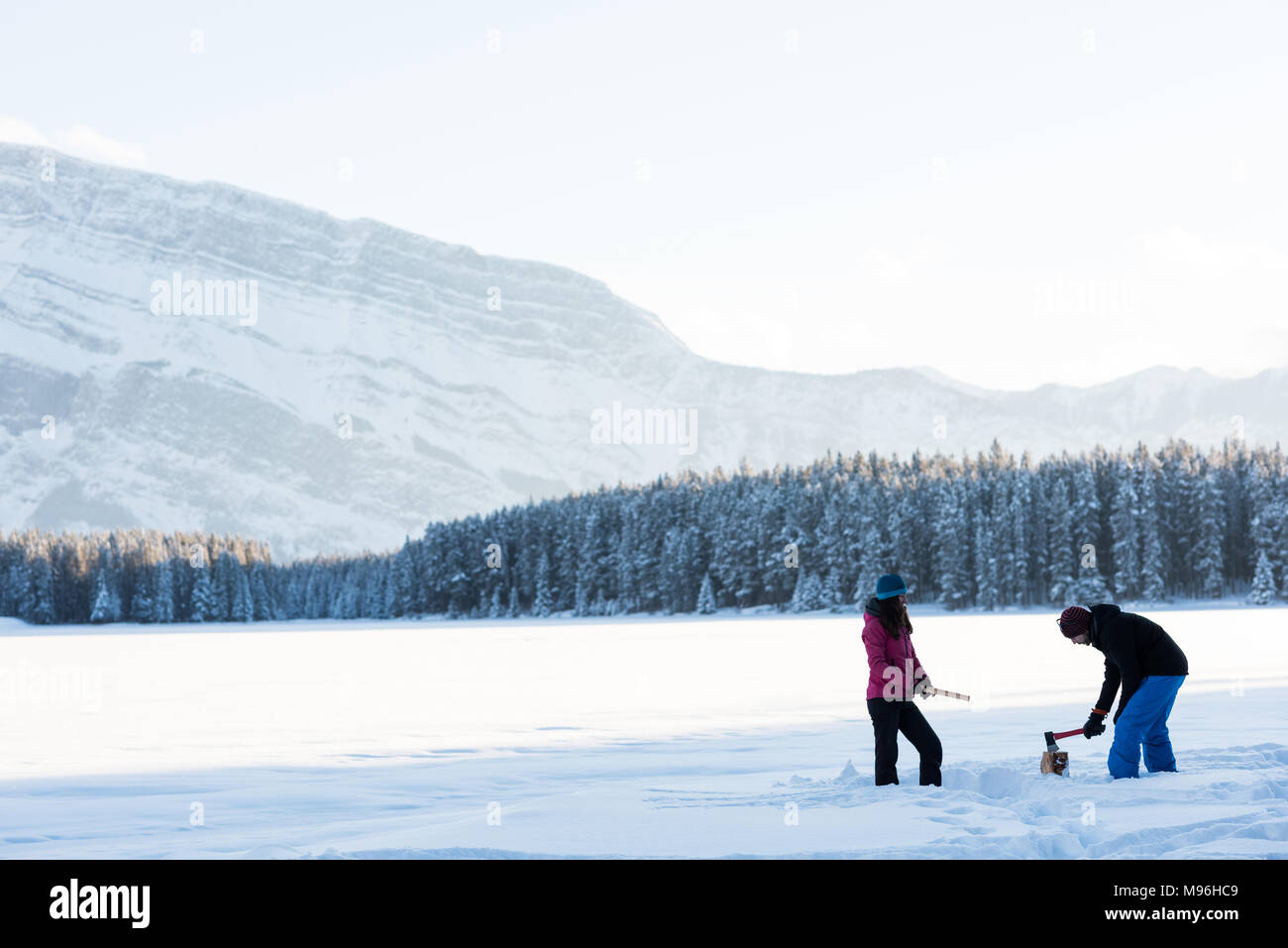 Couple cutting wood with an axe in snowy landscape Stock Photo - Alamy