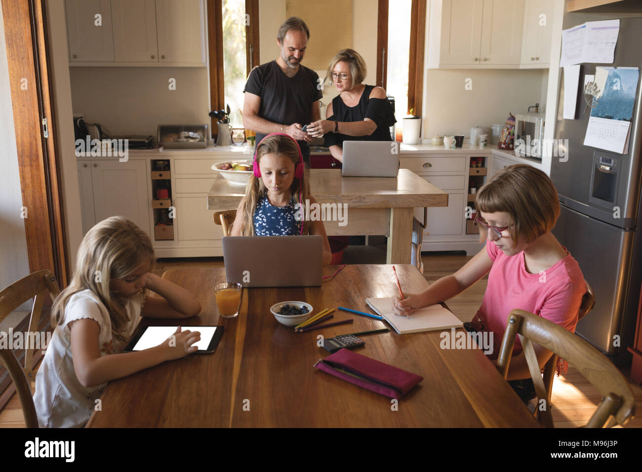Parents using laptop while kids studying in kitchen Stock Photo - Alamy