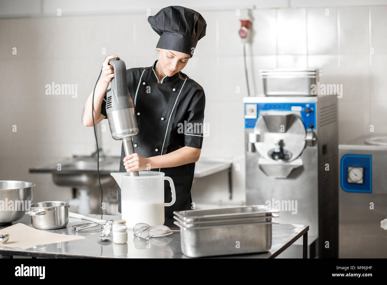 Young woman chef mixing milk with professional blender for ice cream ...