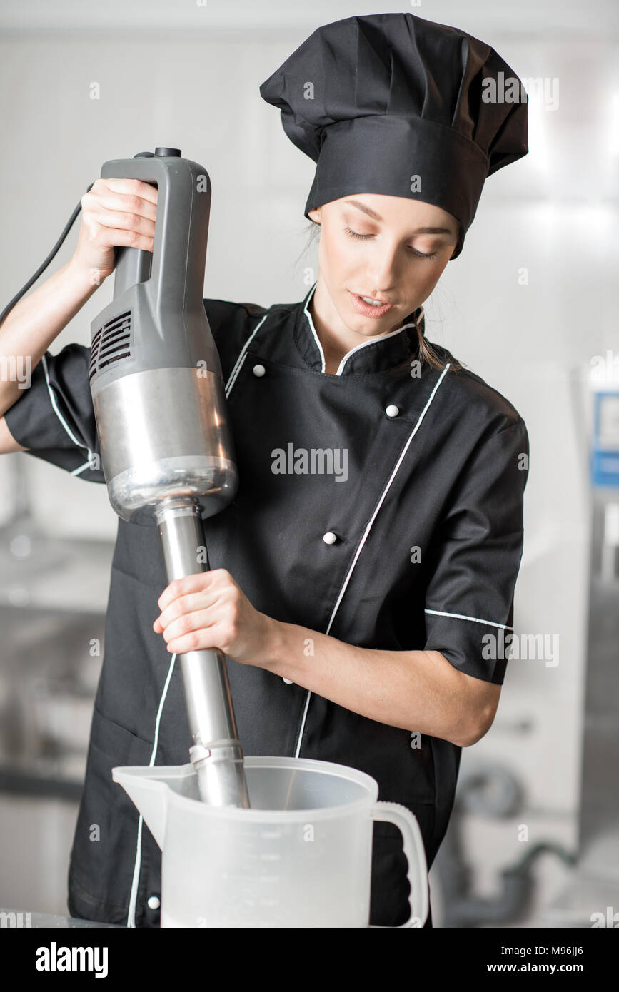 Young woman chef mixing milk with professional blender for ice cream ...