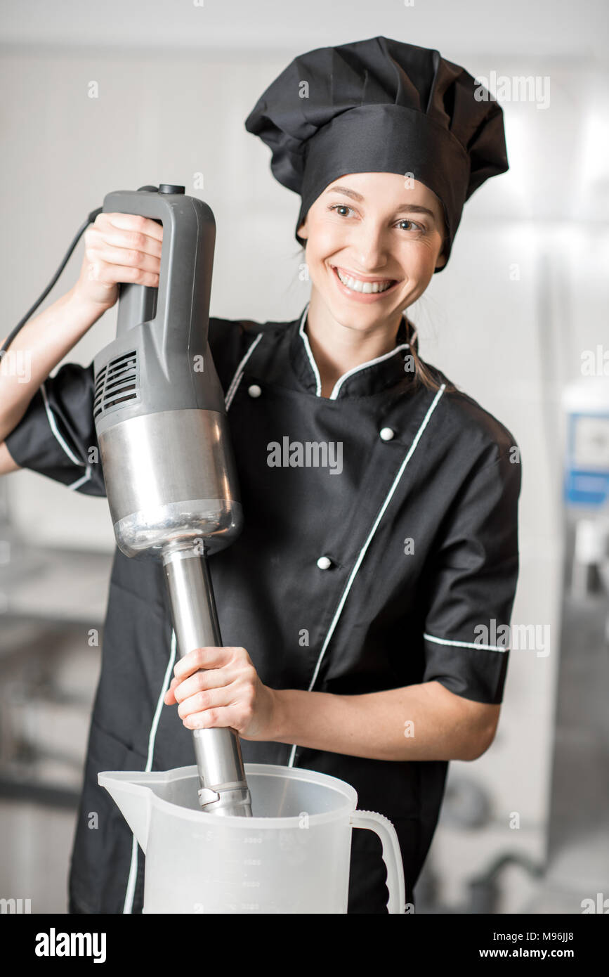 Portrait of a young woman chef mixing milk with professional blender ...