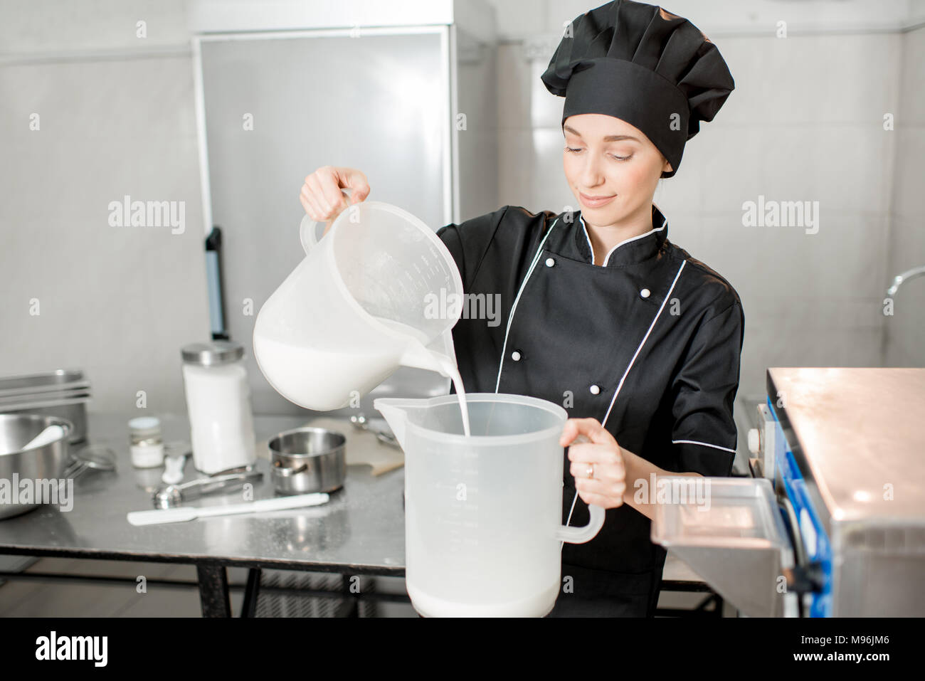 Young woman chef pouring milk prepairing basis for ice cream production ...