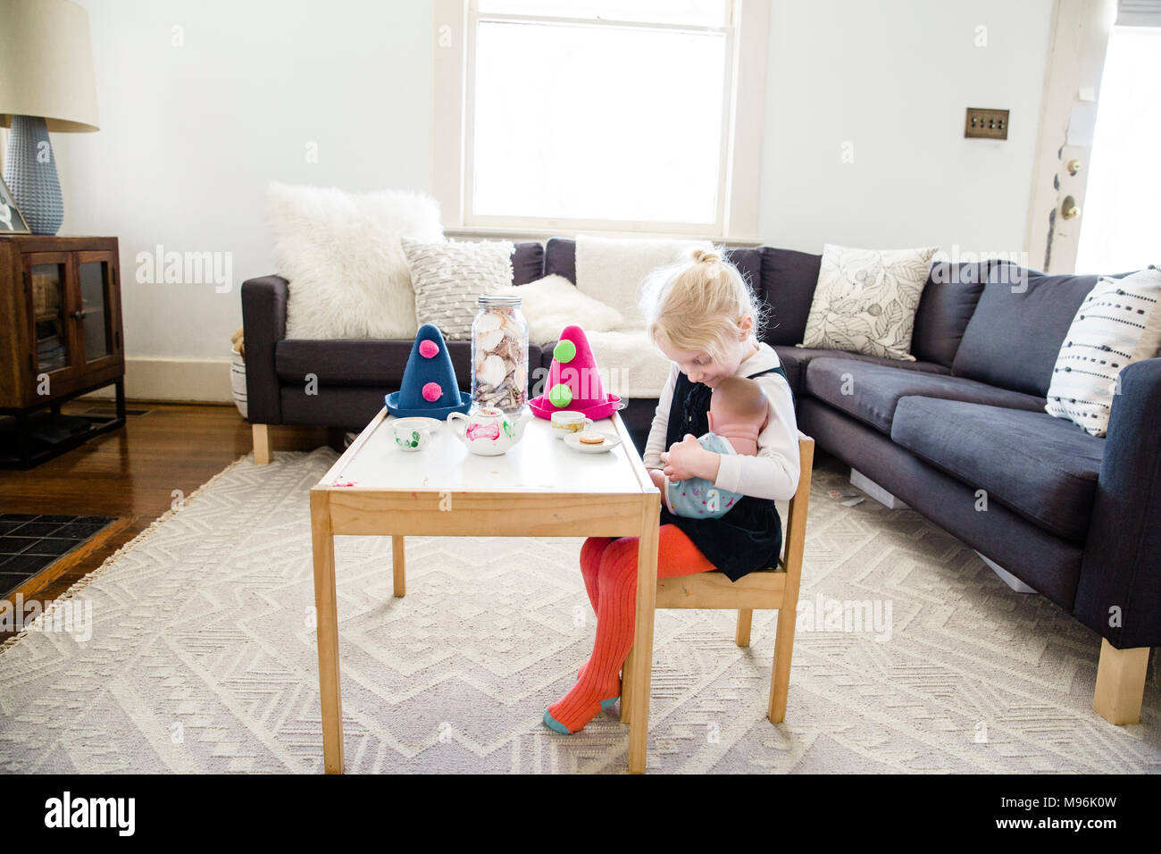 Girl sitting on chair next to table with party hats on Stock Photo - Alamy