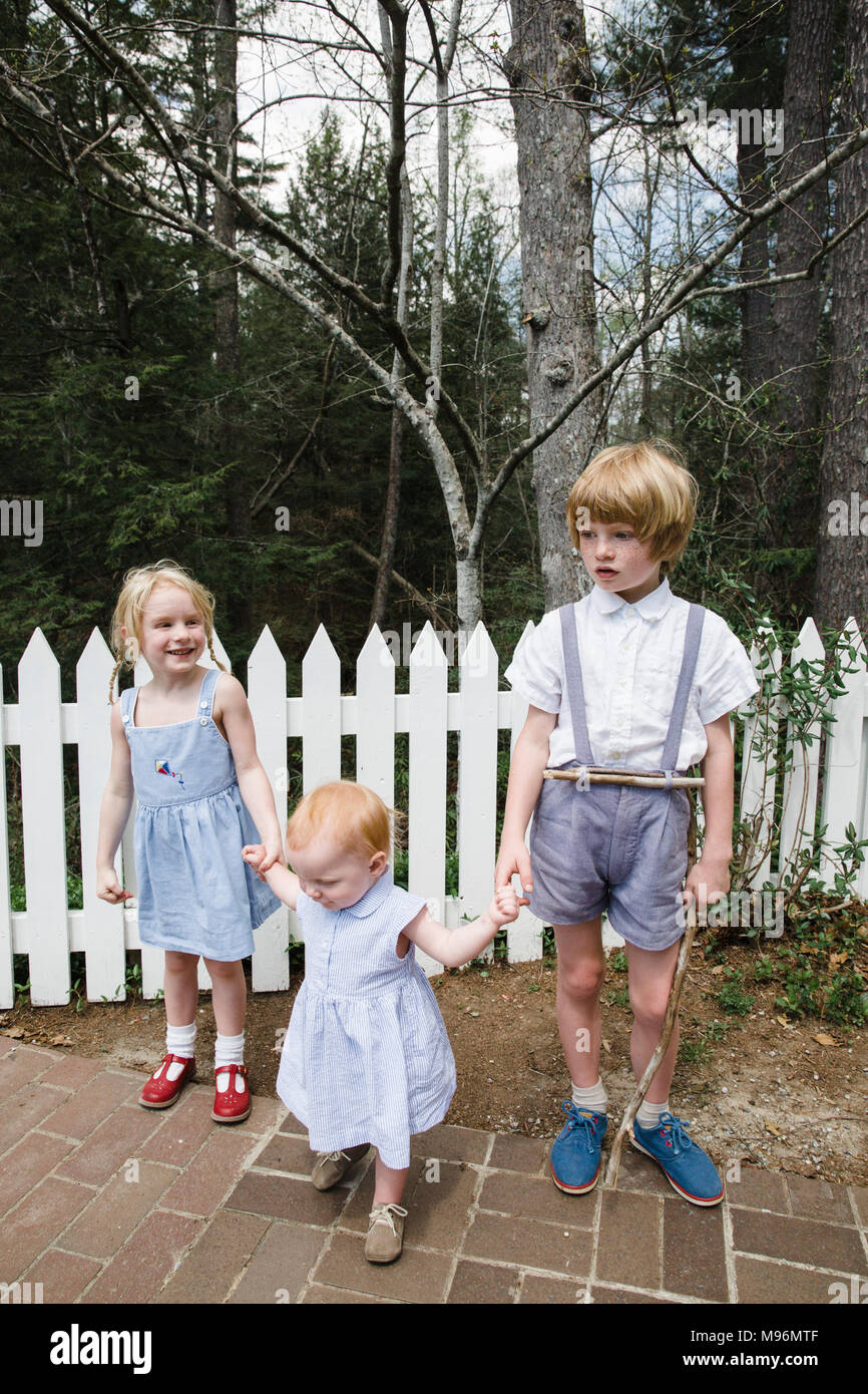Two children holding babies hands next to white fence Stock Photo - Alamy