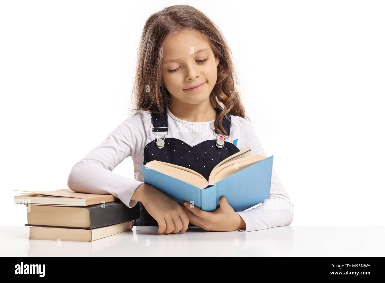 Little girl sitting at a table and reading a book isolated on white ...