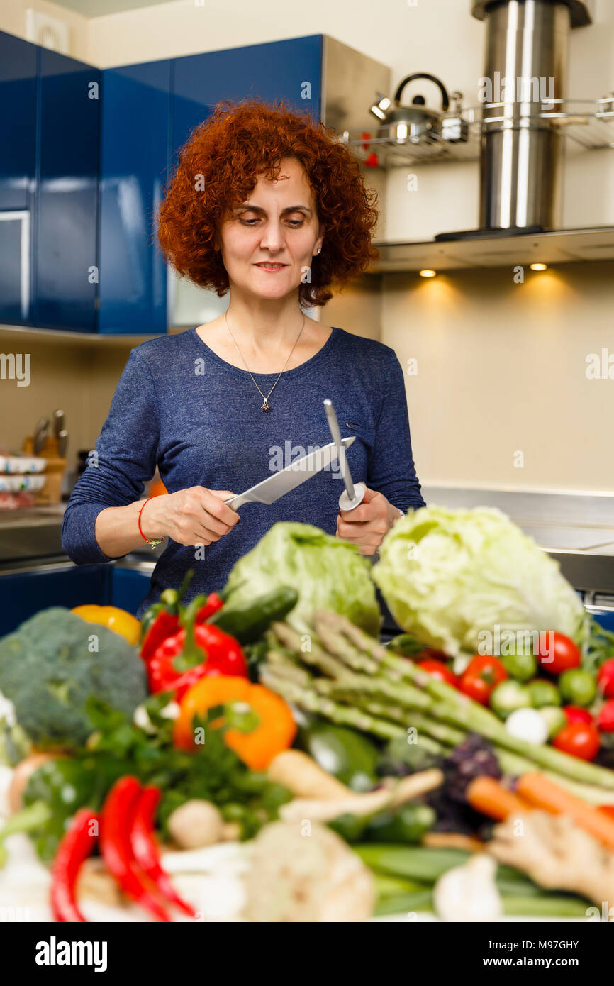 Woman sharpening knife, with a pile of vegetables in front of her Stock ...
