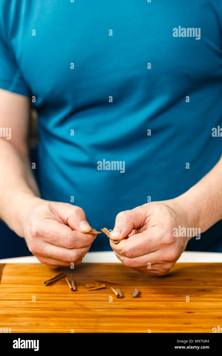 Man breaking a cinnamon stick over a wooden board Stock Photo - Alamy