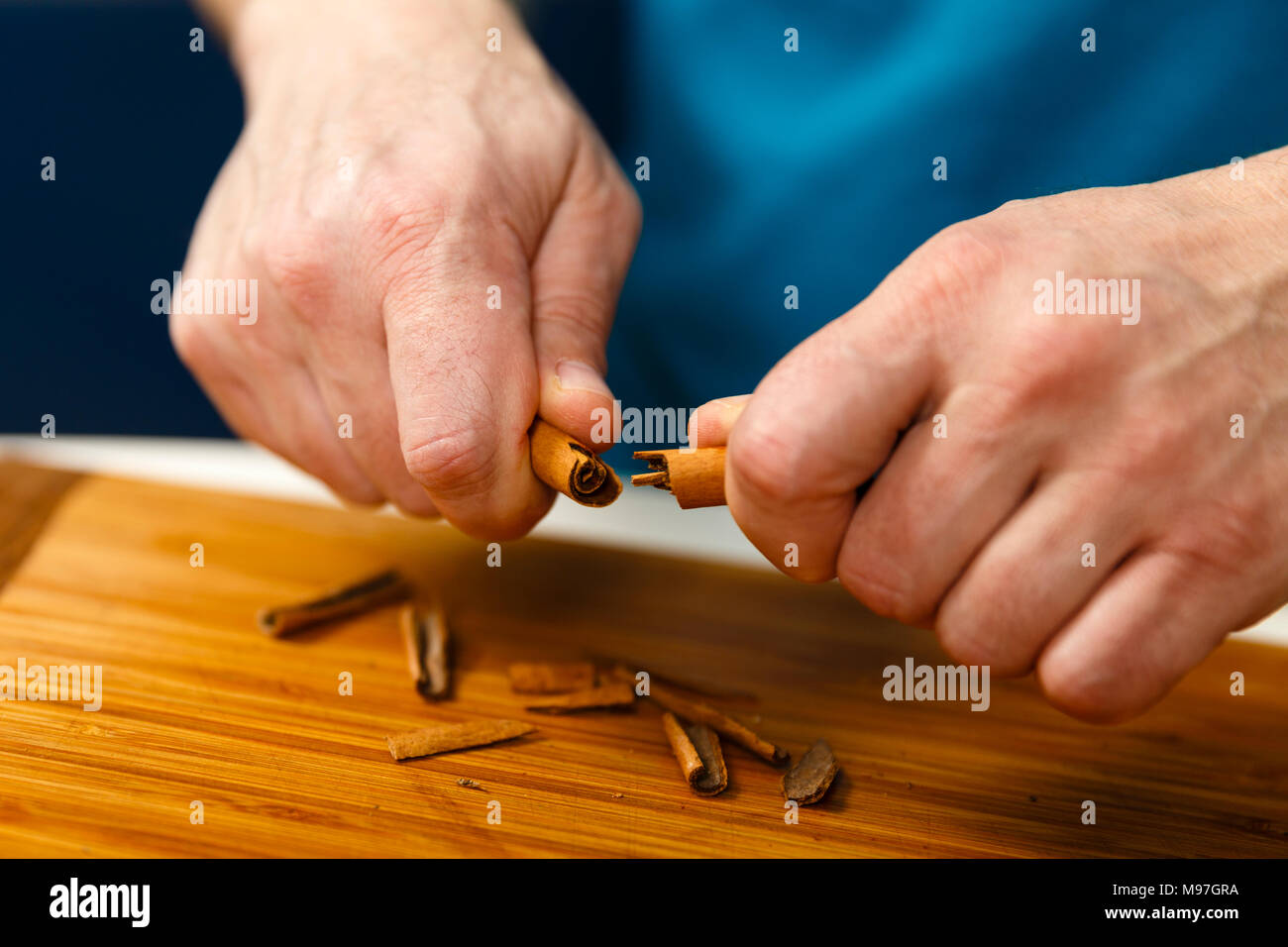 Man breaking a cinnamon stick over a wooden board Stock Photo - Alamy