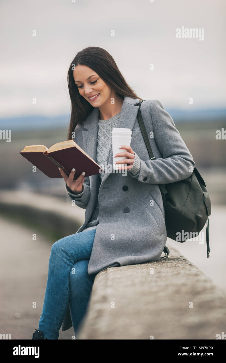 Young woman is reading book and drinking coffee to go after work Stock ...