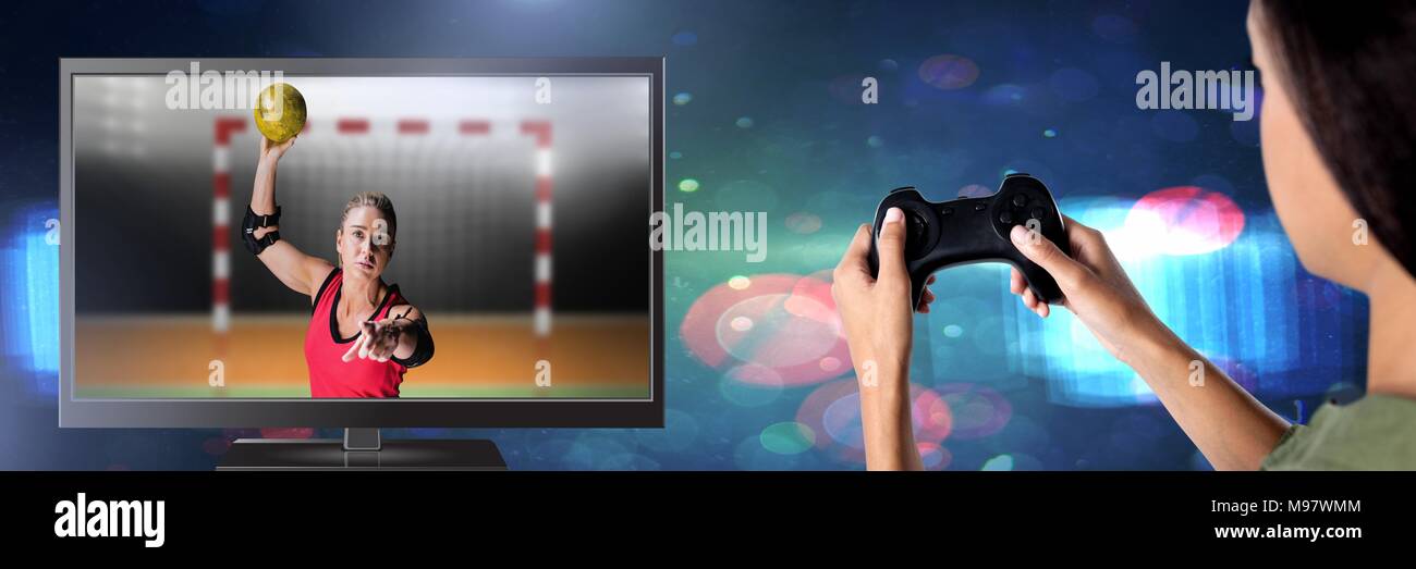 Hands holding gaming controller with handball player on television ...