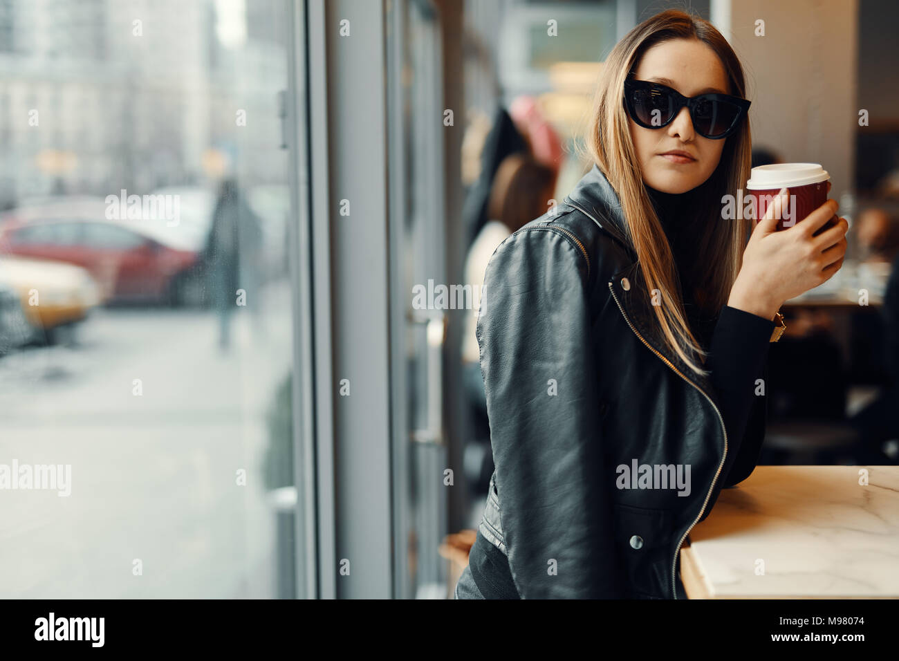 Young girl sit in coffee place in front of the window look at her ...