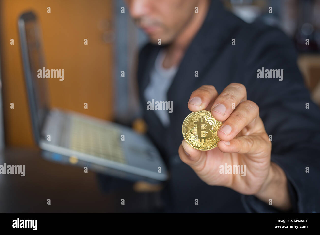 A man holding golden bitcoin while working with laptop Stock Photo - Alamy