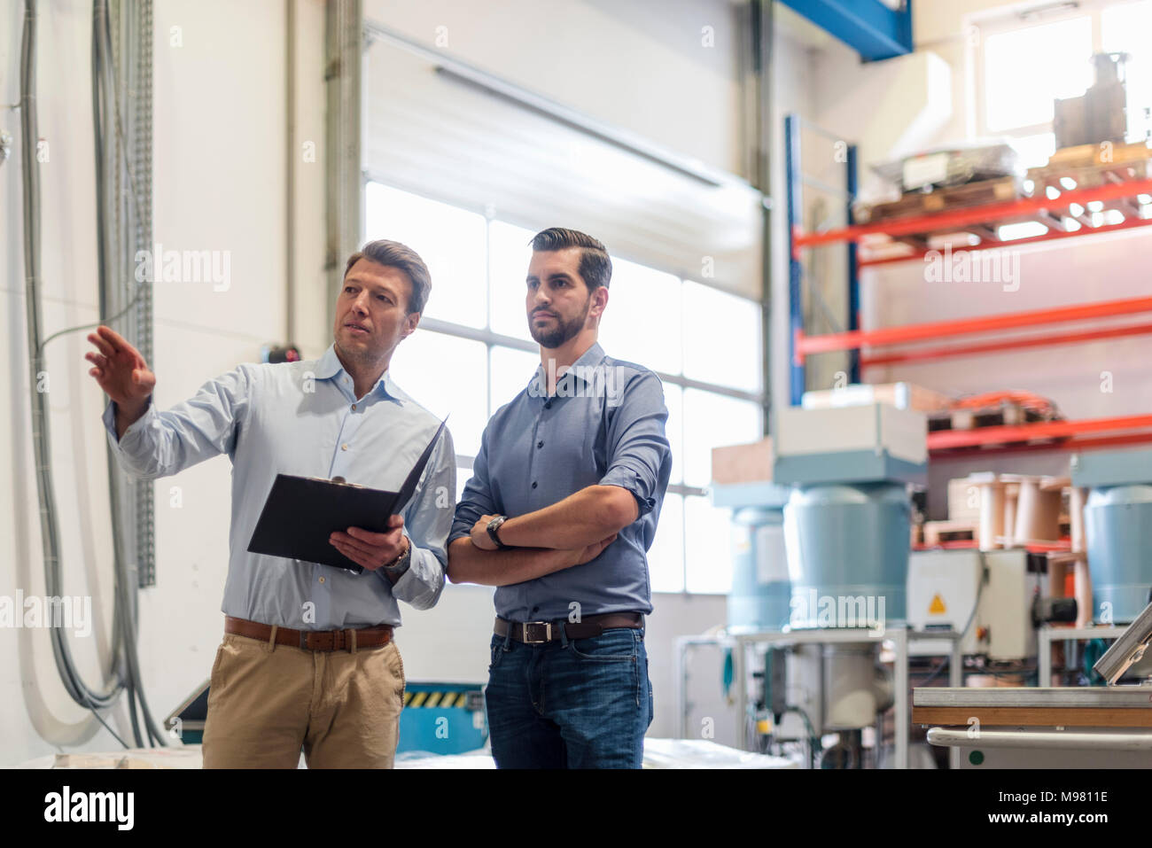 Two men with folder talking in factory storeroom Stock Photo - Alamy