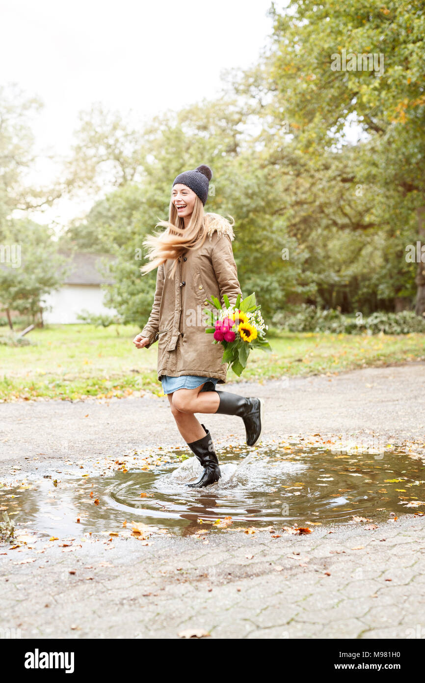 Happy young woman holding bunch of flowers jumping in puddle Stock ...