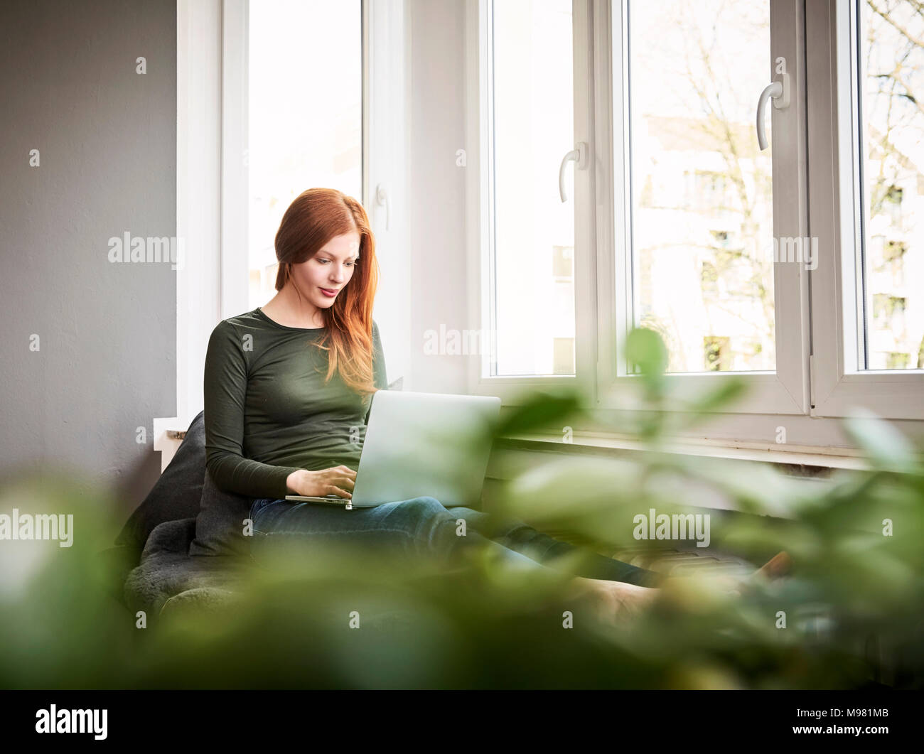 Redheaded woman sitting beside window using laptop Stock Photo - Alamy