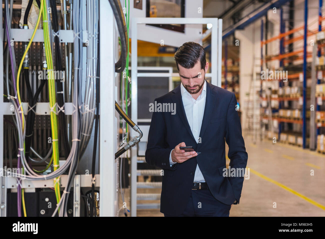Businessman in factory checking cell phone Stock Photo - Alamy