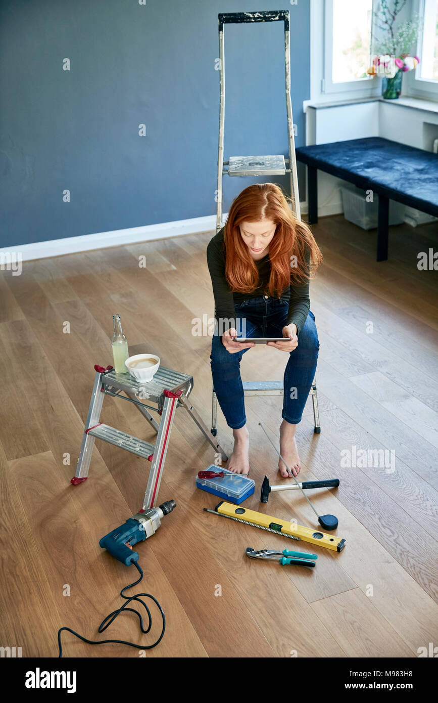 Redheaded woman sitting on step ladder using tablet Stock Photo - Alamy