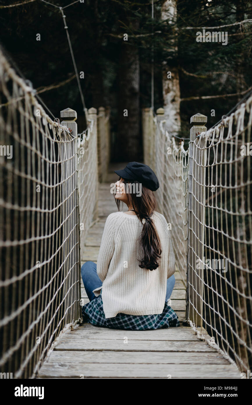 Smiling young woman sitting on a suspension bridge Stock Photo - Alamy