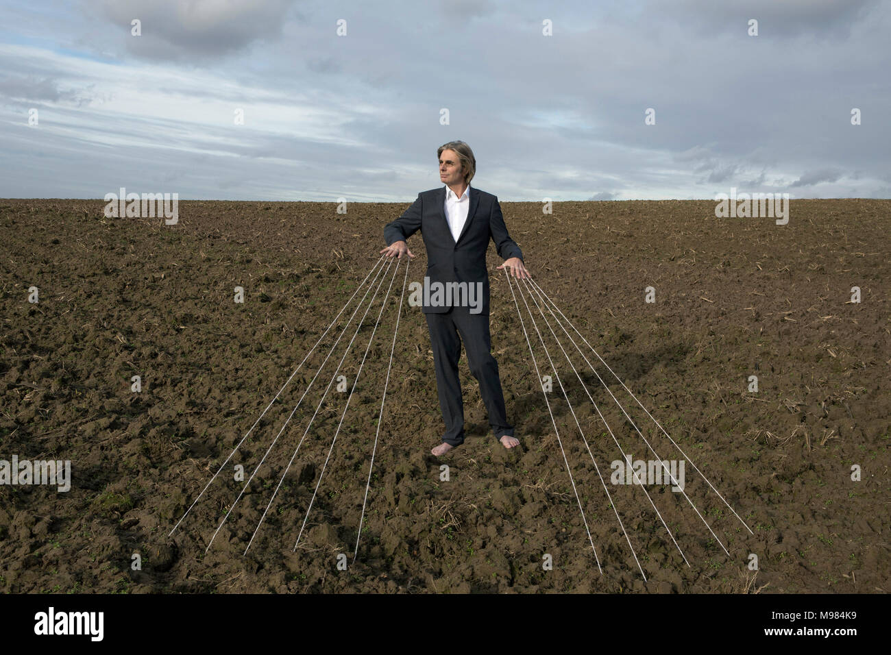 Businessman standing on a field tied to strings Stock Photo - Alamy