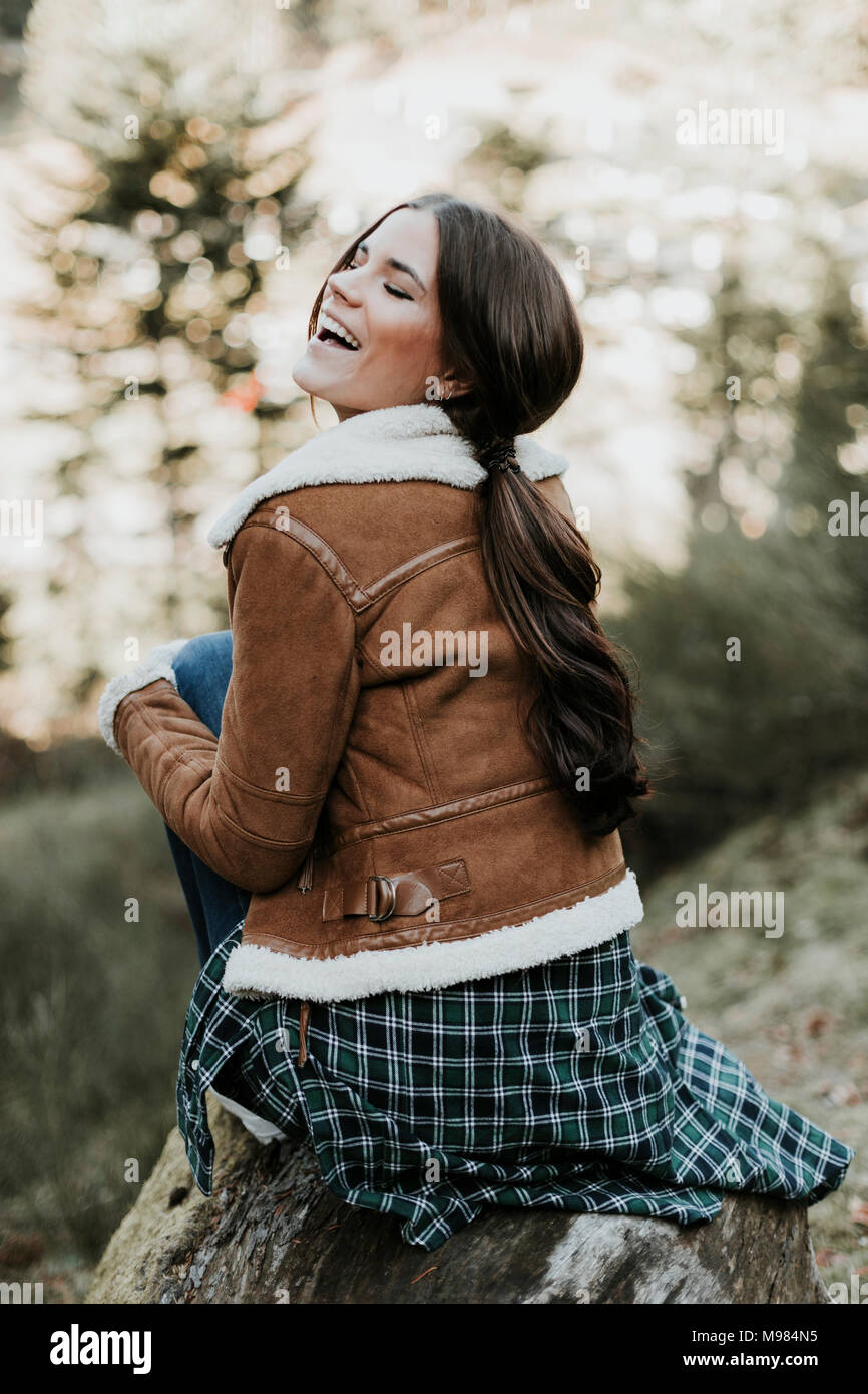 Woman laughing and sitting on log with dog Stock Photo - Alamy