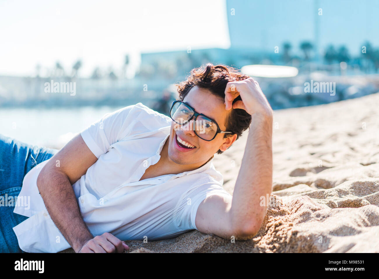 Portrait of happy young man lying in sand on the beach Stock Photo - Alamy