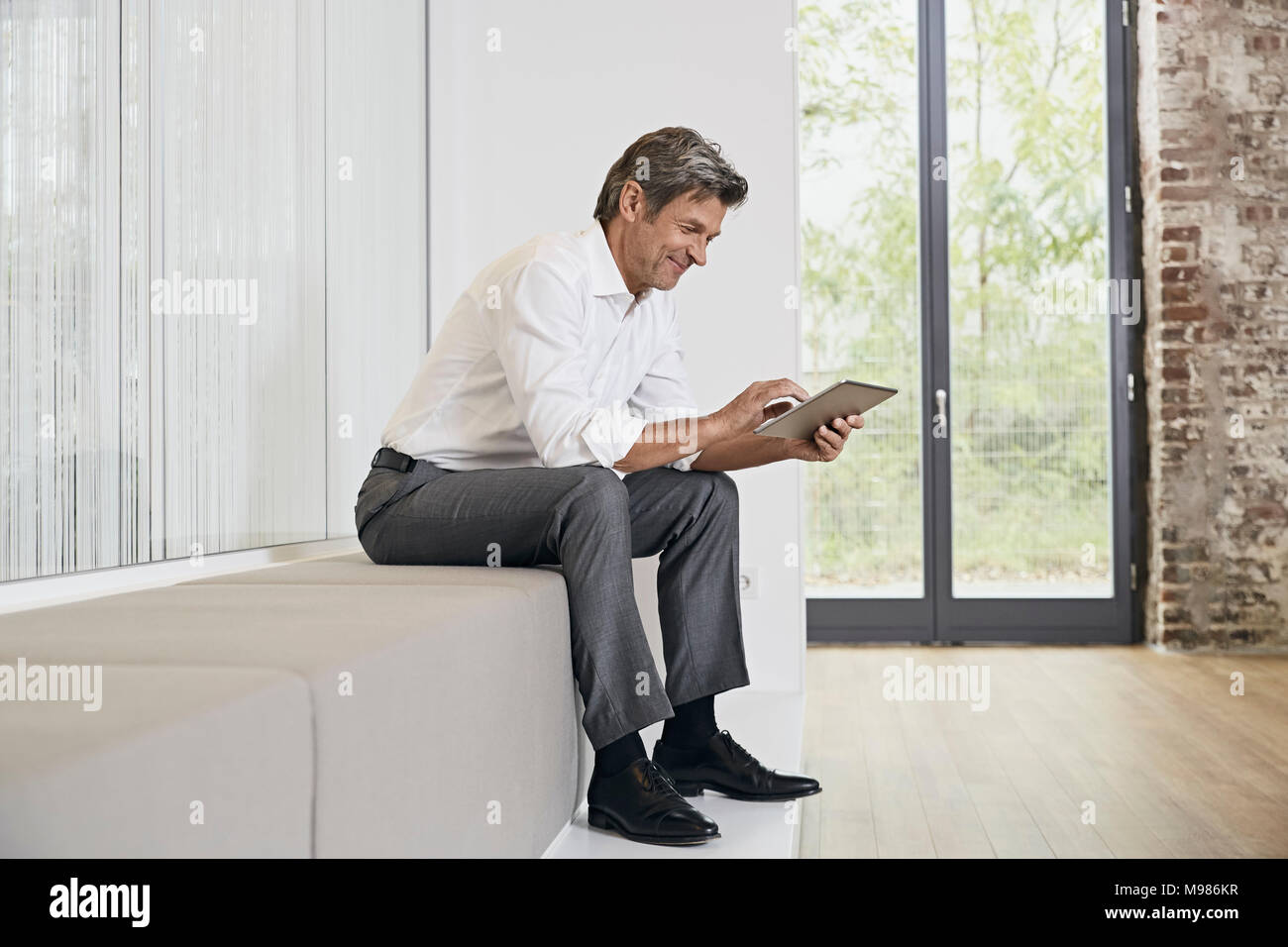 Businessman sitting on bench in modern office using tablet Stock Photo ...