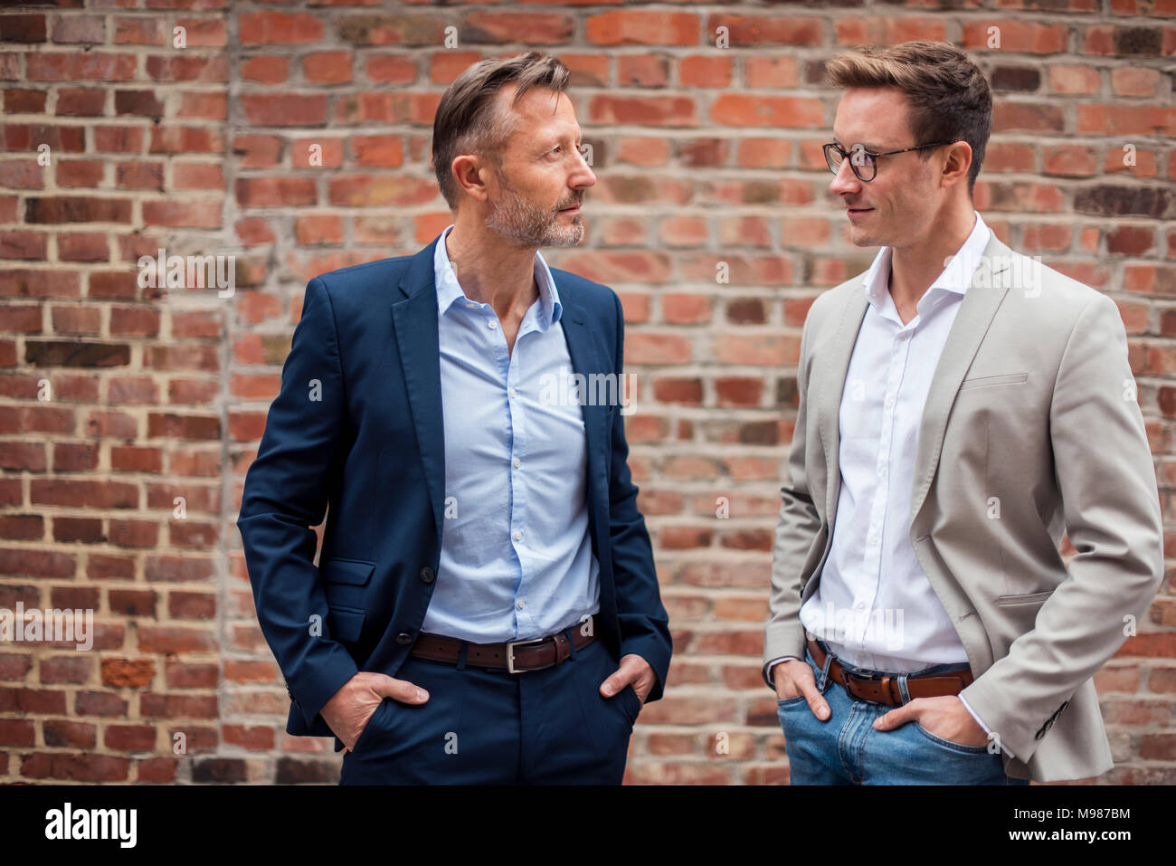 Two businessmen standing at brick building Stock Photo - Alamy