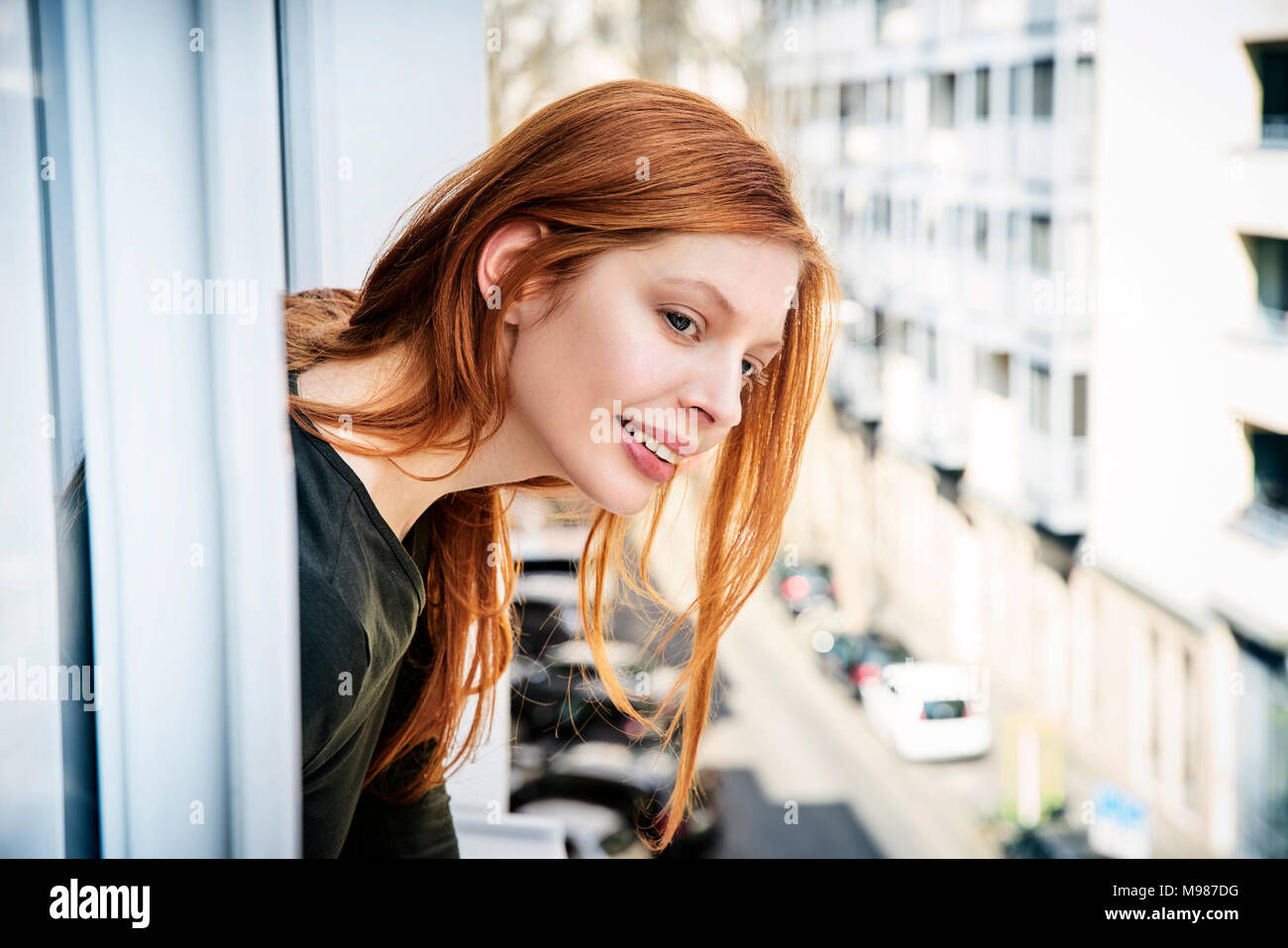 Portrait of smiling redheaded woman leaning out of window Stock Photo ...
