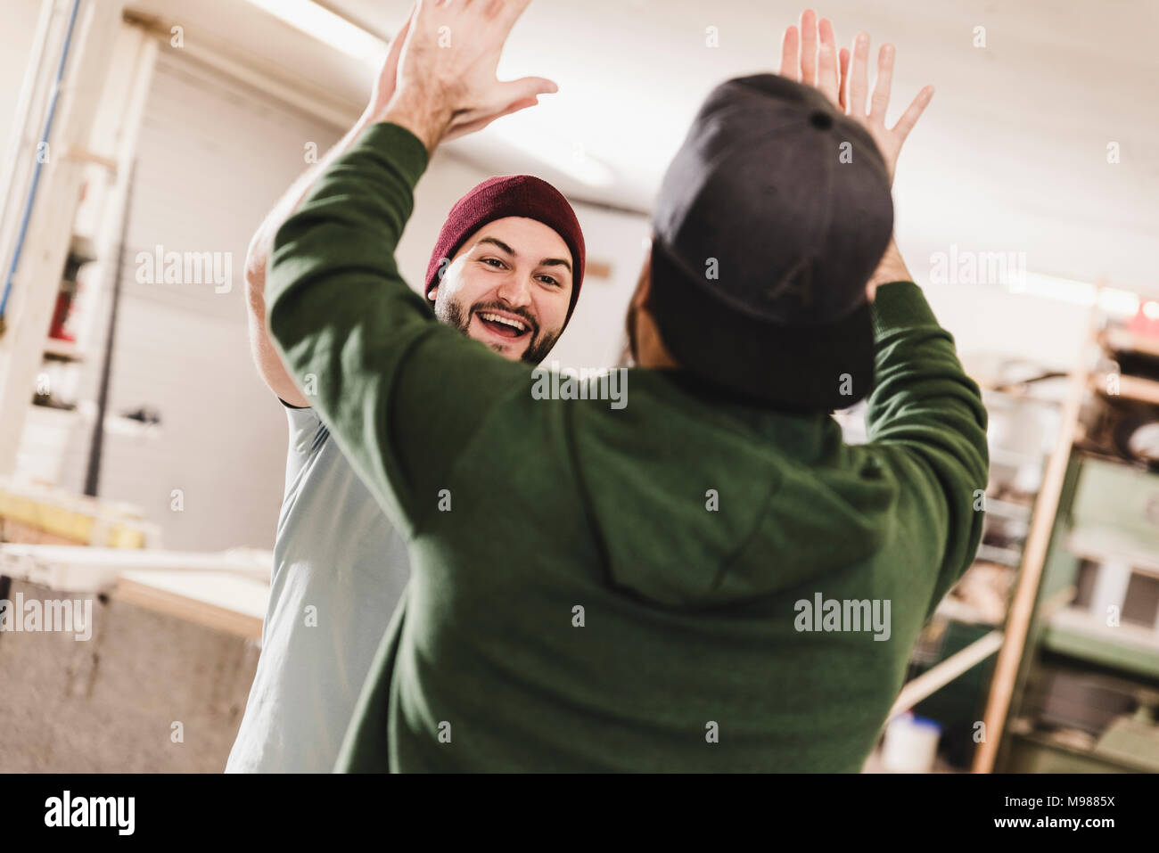 Two happy young men high fiving in workshop Stock Photo - Alamy